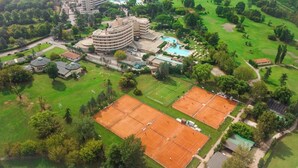Vista aérea de um resort com um grande edifício circular, quadras de tênis e uma piscina.