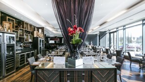 Restaurante moderno com área de bar central, prateleiras de vinho e diferentes opções de assentos.