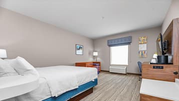 Quarto de hotel com cama, escrivaninha, cadeira, janela e obras de arte na parede.
