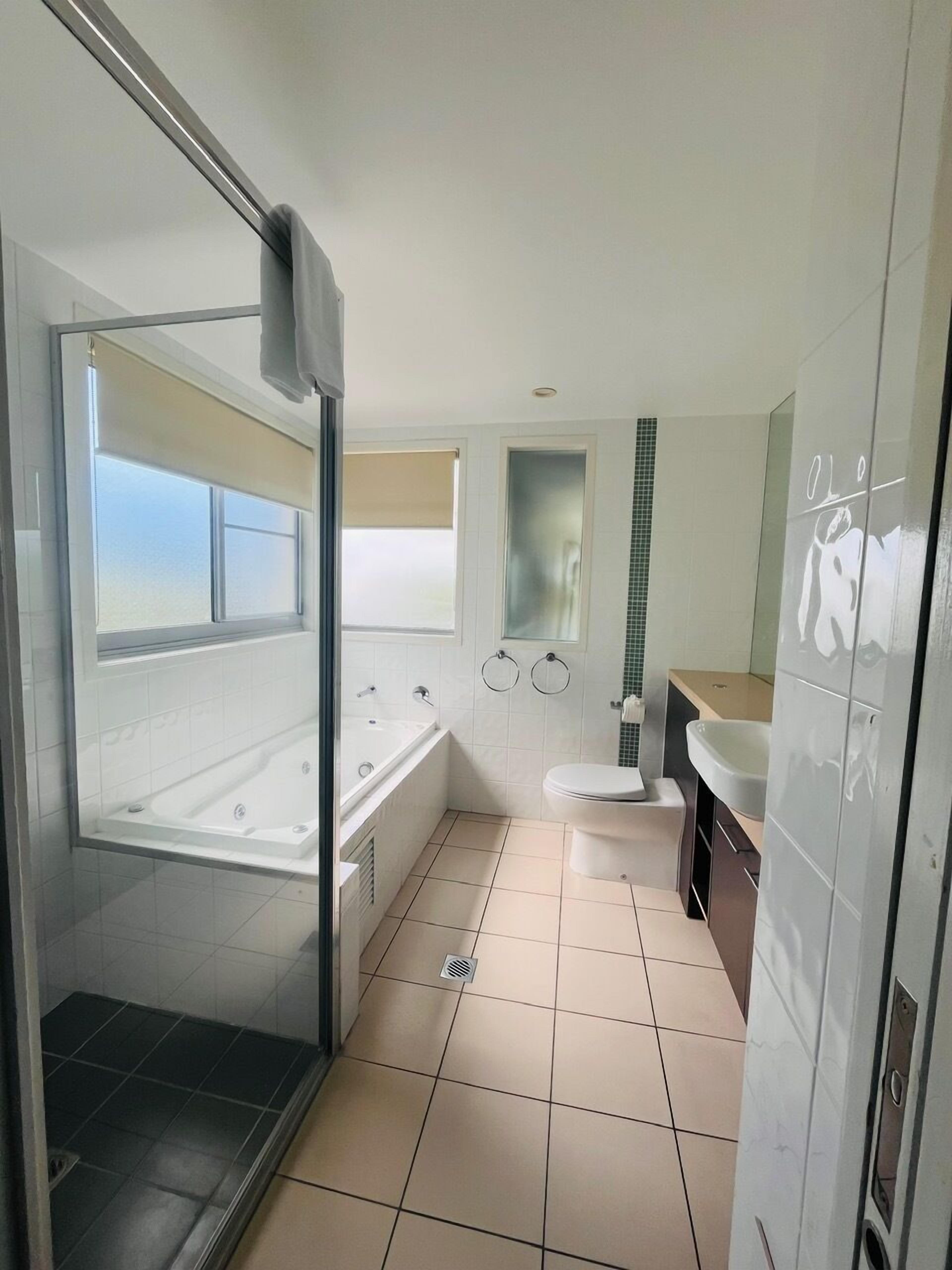 Uma casa de banho moderna com cabine de duche em vidro, banheira, sanita e lavatório.