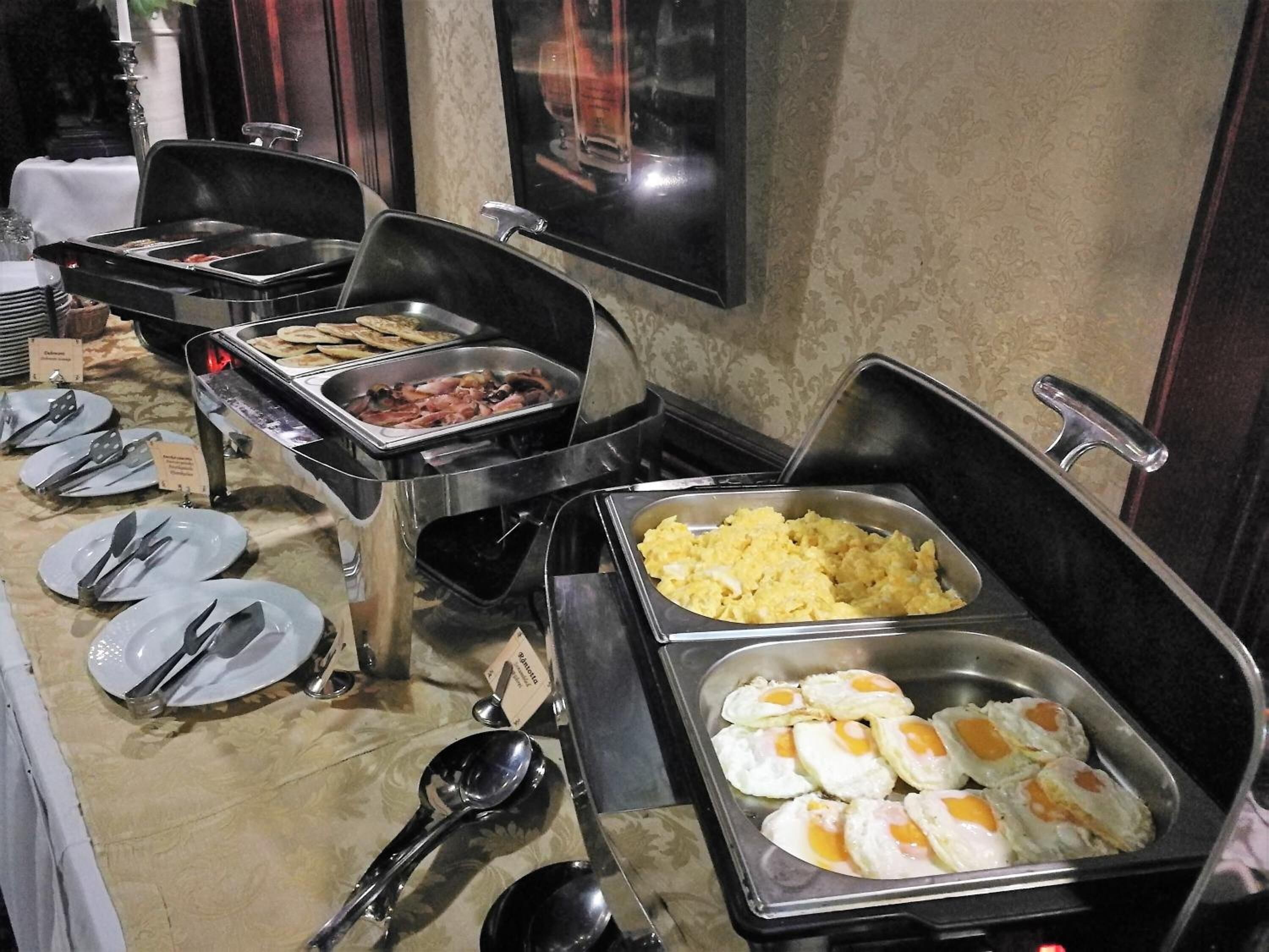 Buffet com diversos alimentos, como ovos mexidos, bacon e batatas.