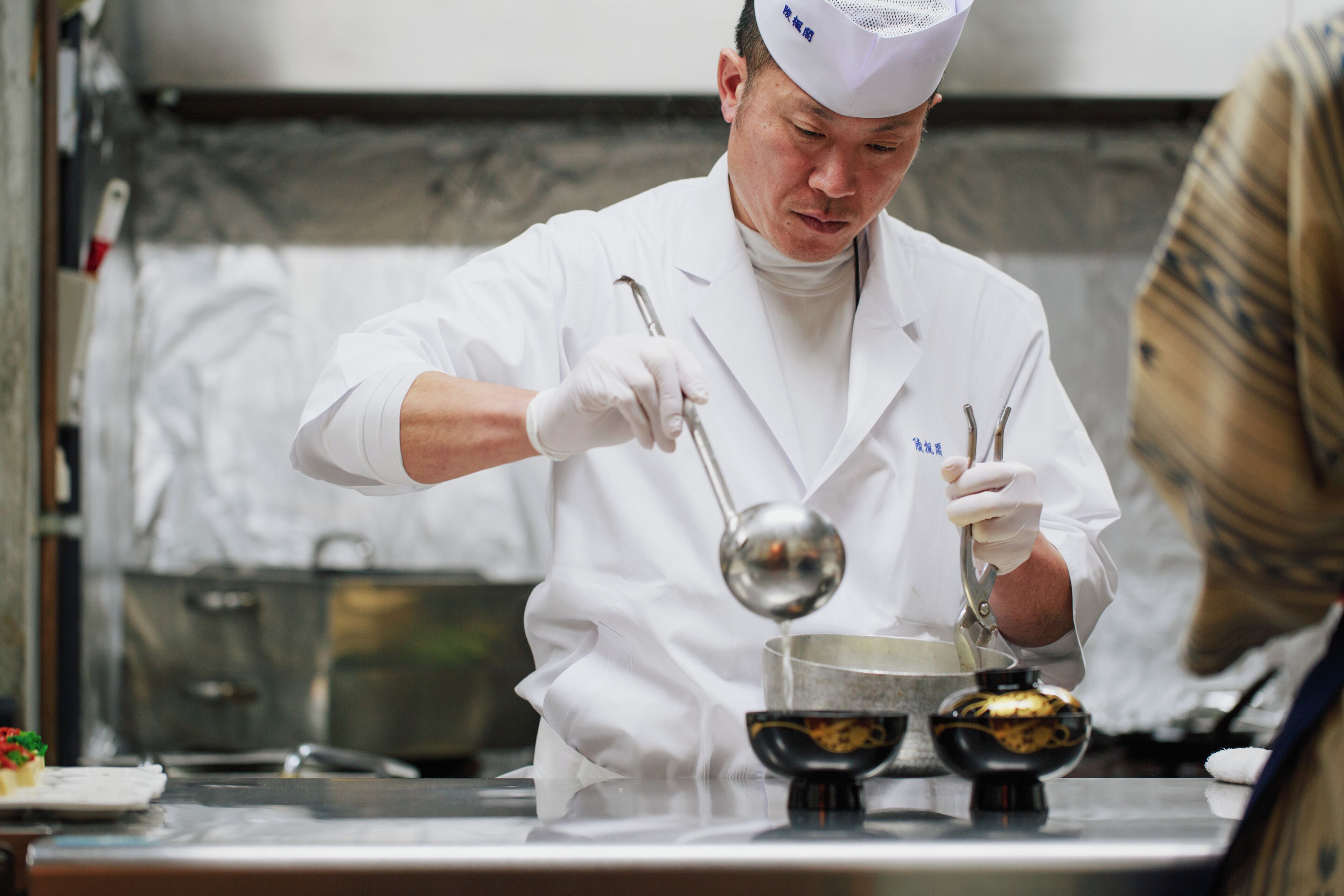 Um chefe de cozinha de uniforme branco preparando alimentos em uma cozinha profissional.