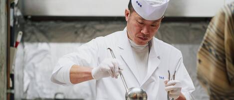 Um chefe de cozinha de uniforme branco preparando alimentos em uma cozinha profissional.
