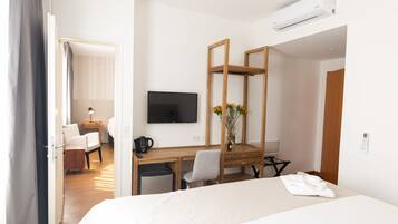 Quarto de hotel com uma cama, uma escrivaninha com cadeira, uma televisão e um espelho.