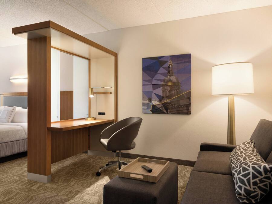 Quarto de hotel com cama, escrivaninha, cadeira, sofá, luminária e um quadro na parede.