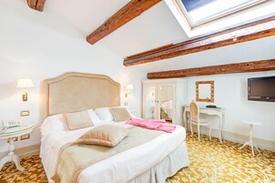 Quarto de hotel com cama, mesa de cabeceira, abajur, escrivaninha, cadeira e televisão.