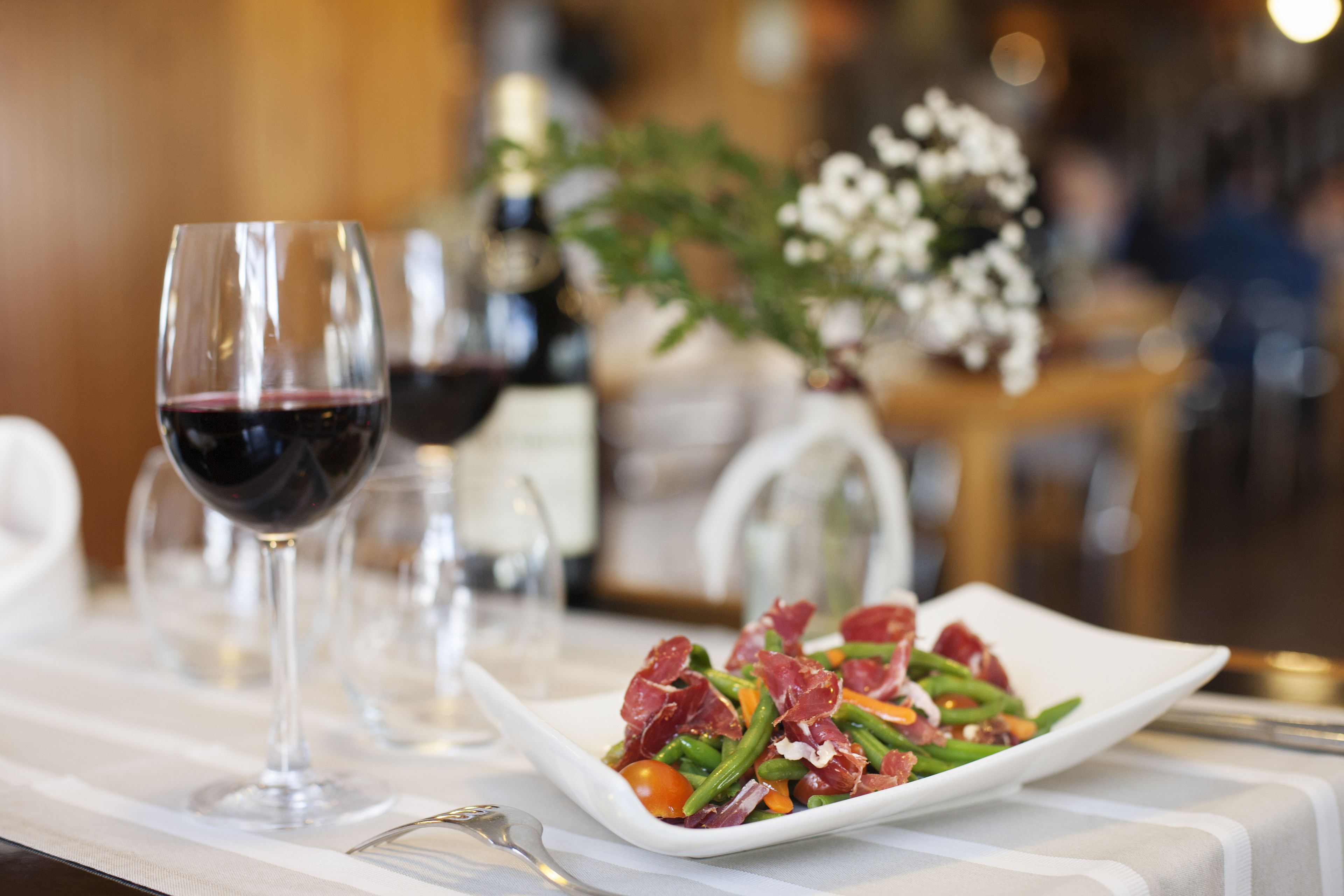 Uma mesa de jantar com um prato de comida branco, copos de vinho e um vaso com flores.
