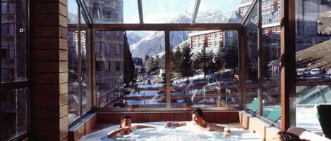 Quarto de hotel moderno com uma grande janela que oferece vista para uma montanha nevada e para a paisagem urbana.