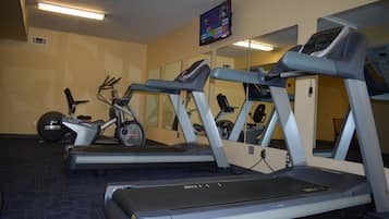 Uma academia com esteiras, bicicletas ergométricas e um espelho grande.