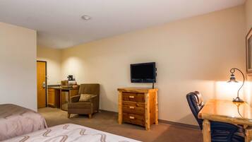 Quarto de hotel com duas camas, uma escrivaninha com cadeira, televisão e cozinha compacta.