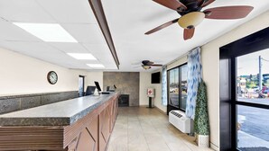 Uma área de recepção com lareira de pedra, um relógio, um ventilador de teto e uma janela grande com vista para a rua.