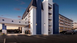 Um hotel moderno com uma torre central, várias varandas e uma área de entrada coberta.