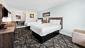 Quarto de hotel com duas camas, uma escrivaninha, um espelho e uma janela.