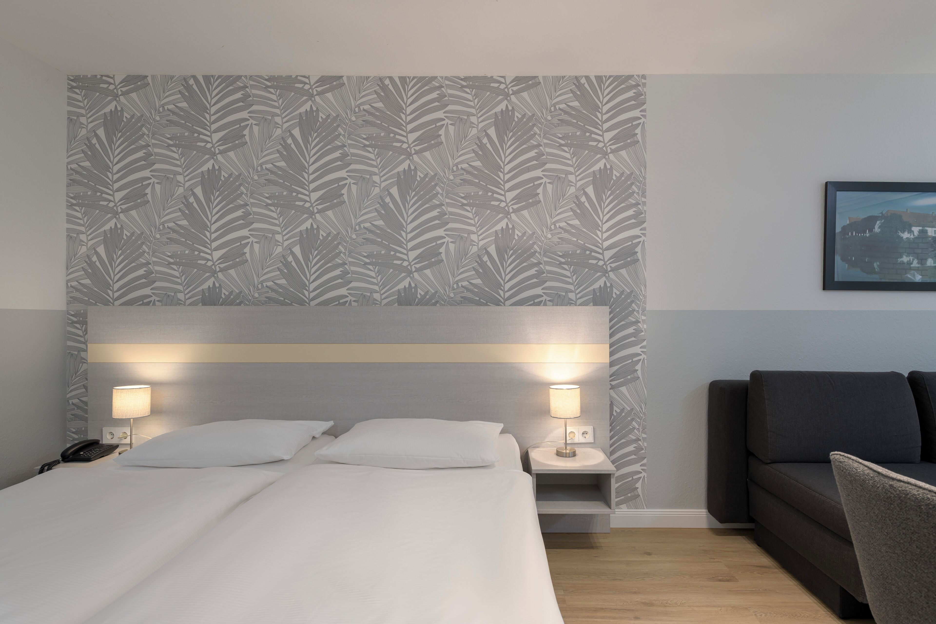 Quarto de hotel com cama, abajures, mesa de cabeceira, sofá e quadro na parede.