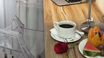 Uma mesa de madeira com um laptop, uma chávena de café, uma rosa e fruta.