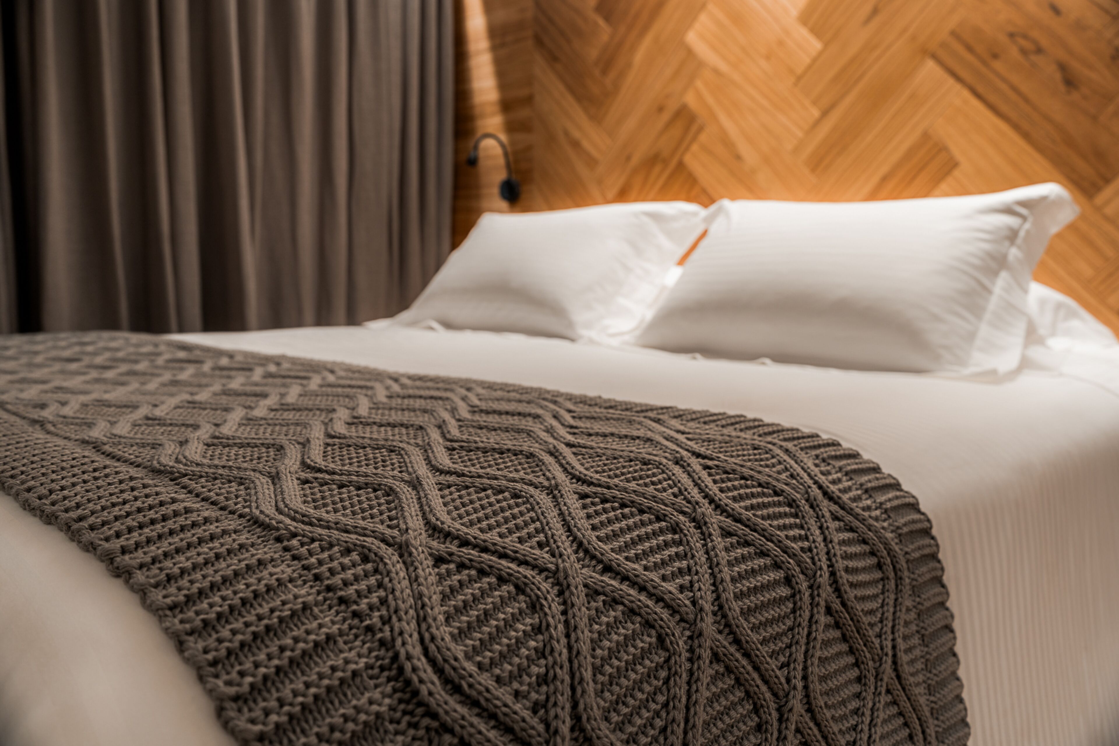 Cama bem arrumada com manta estampada, travesseiros brancos e cabeceira de madeira.