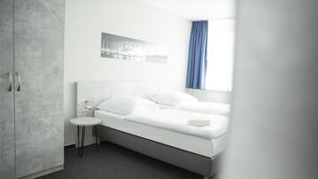 Quarto de hotel moderno com cama, mesa de cabeceira pequena, guarda-roupa e um quadro na parede.