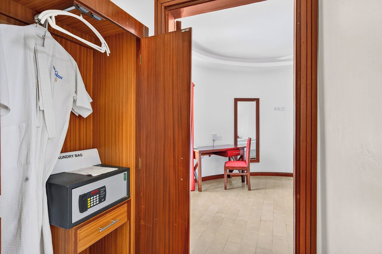 Quarto com guarda-roupa de madeira, uma escrivaninha com cadeira e uma cesta de roupa suja no chão.
