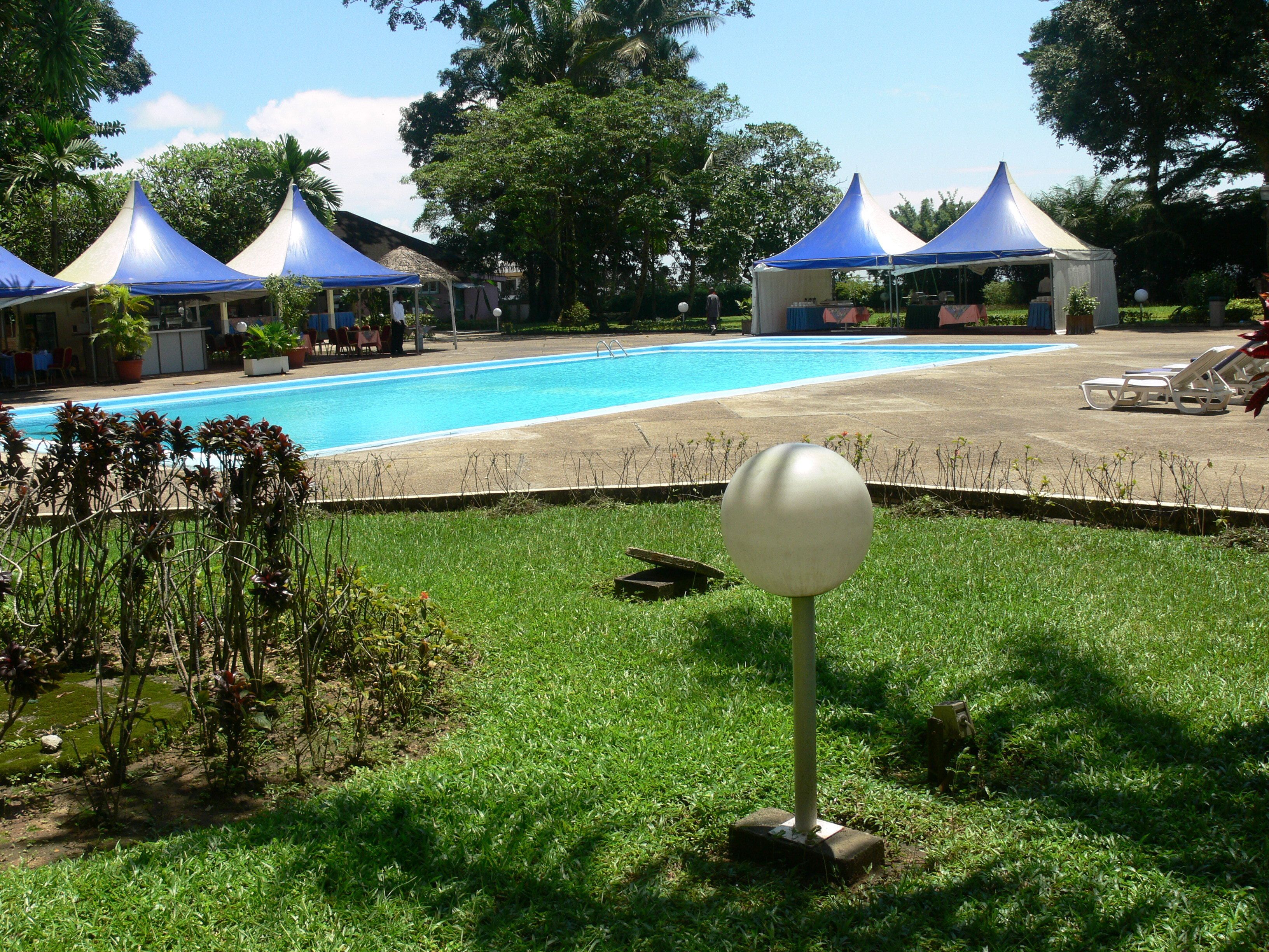 Piscina com tendas azuis e cadeiras de descanso ao fundo.