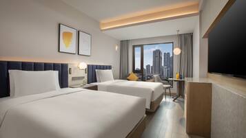 Quarto de hotel com duas camas, uma escrivaninha, televisão e vista para a cidade.