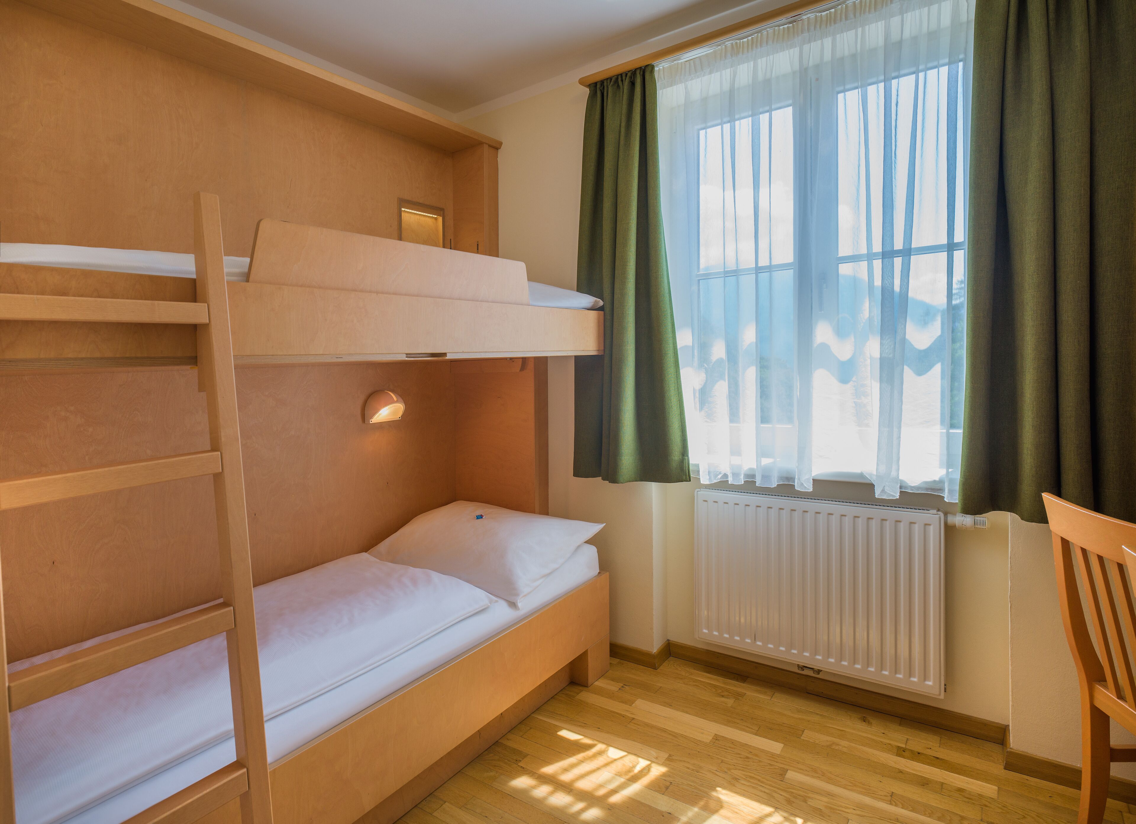 Quarto com beliche, janela, cortinas e radiador.