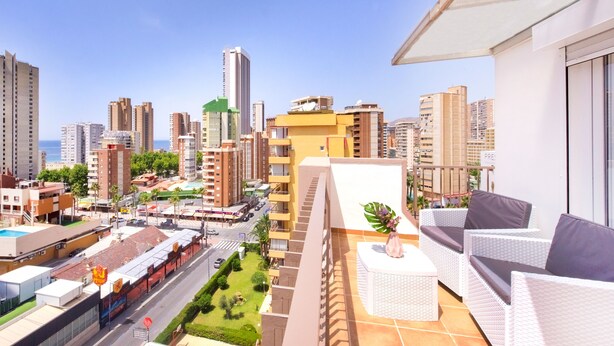 Um edifício alto com varanda, mobiliário externo e vista para a paisagem urbana.