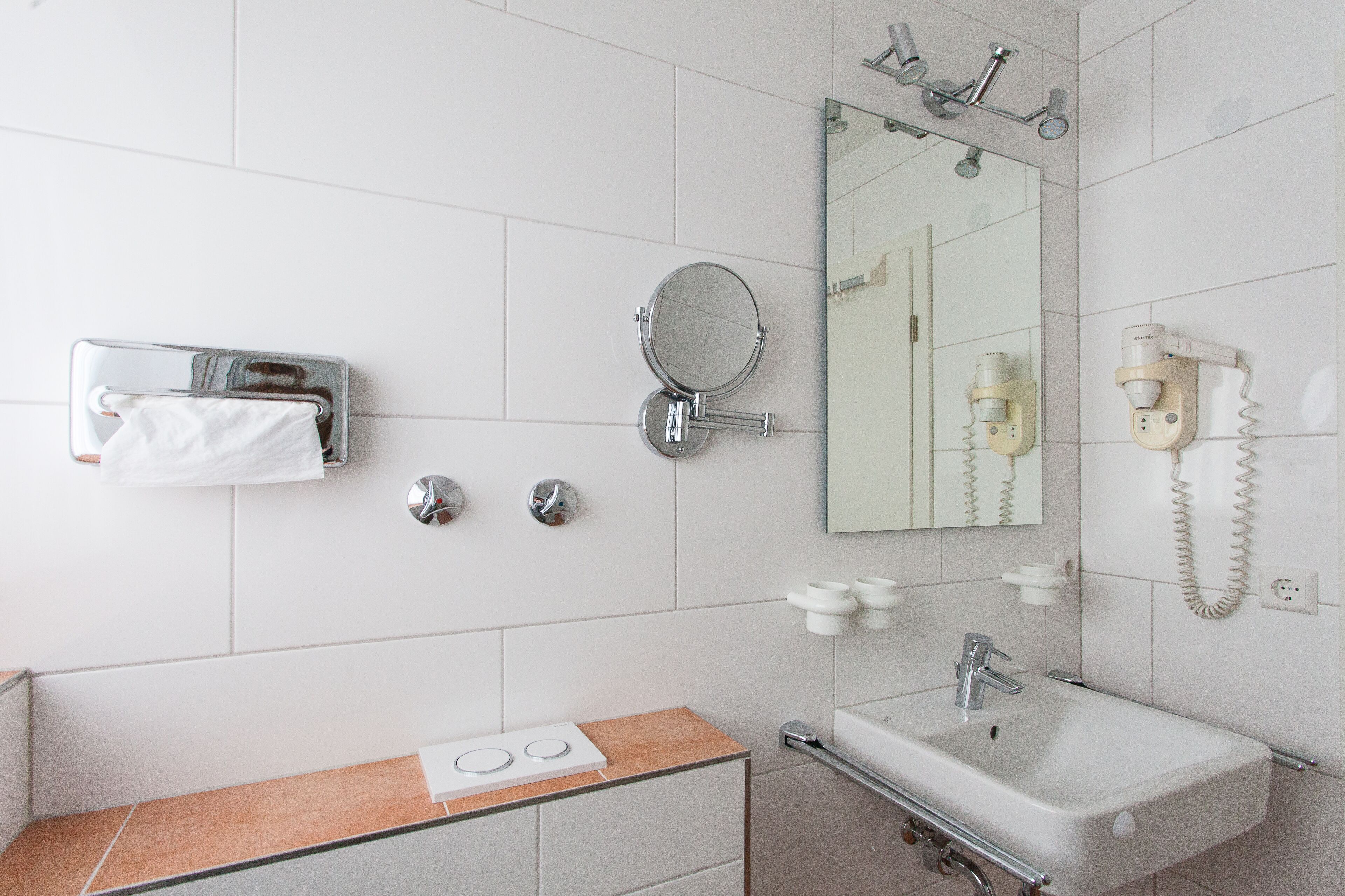 Uma casa de banho moderna com lavatório, espelho, dispensador de toalhas e secador de cabelo.