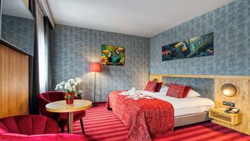 Quarto de hotel com cama, escrivaninha, cadeira, luminária e obras de arte nas paredes.