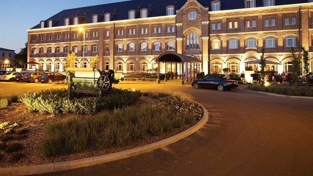 Um hotel grande e histórico com um pátio central, entrada coberta e fachada bem iluminada.