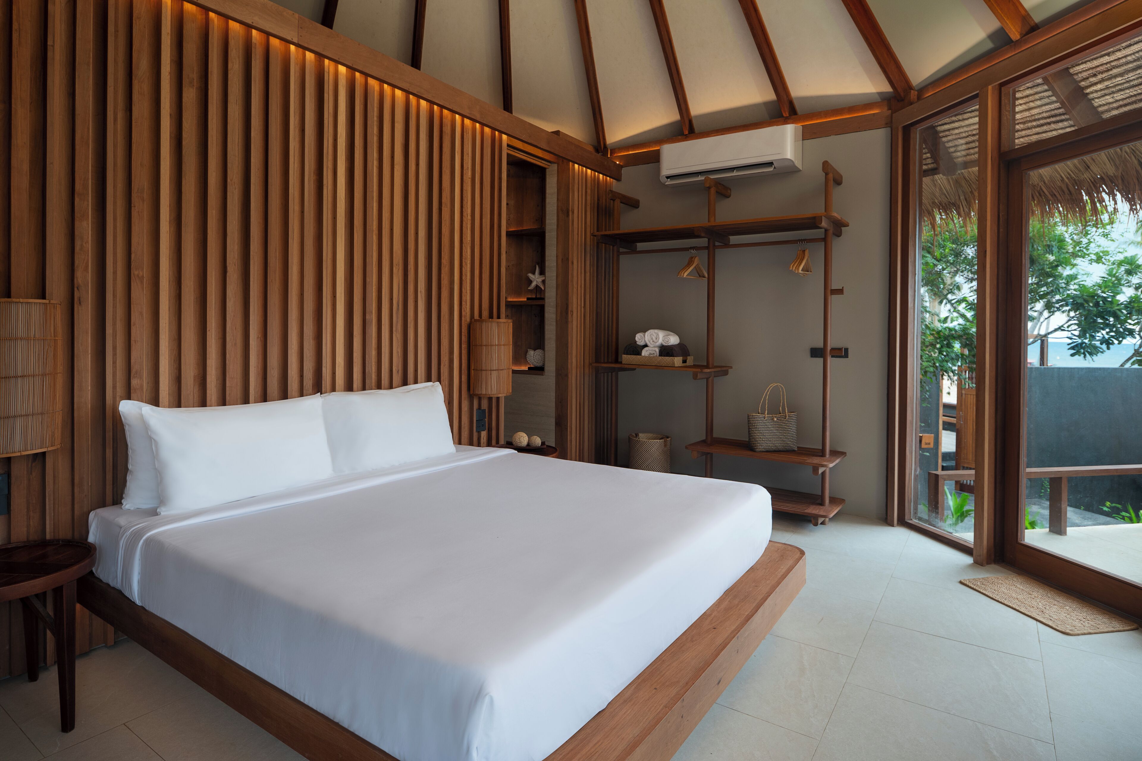 Quarto moderno com uma cama grande, painéis de madeira, guarda-roupa embutido e vista através de uma porta de vidro.