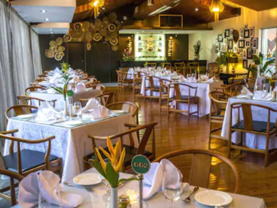 Um restaurante com várias mesas preparadas para refeições, com toalhas de mesa brancas e louças bem organizadas.