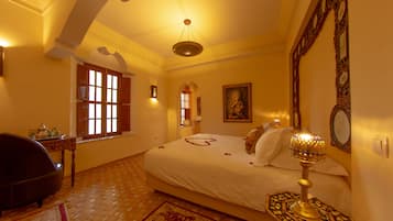 Quarto de hotel com cama, mesa de cabeceira, cadeira, janela com persianas e um objeto decorativo na parede.