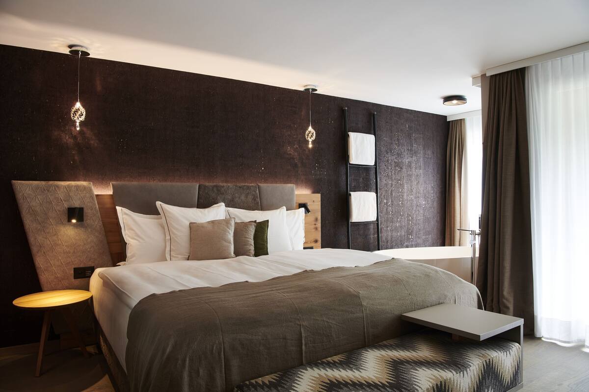 Quarto de hotel moderno com uma cama grande, mesas de cabeceira e um banco embutido.