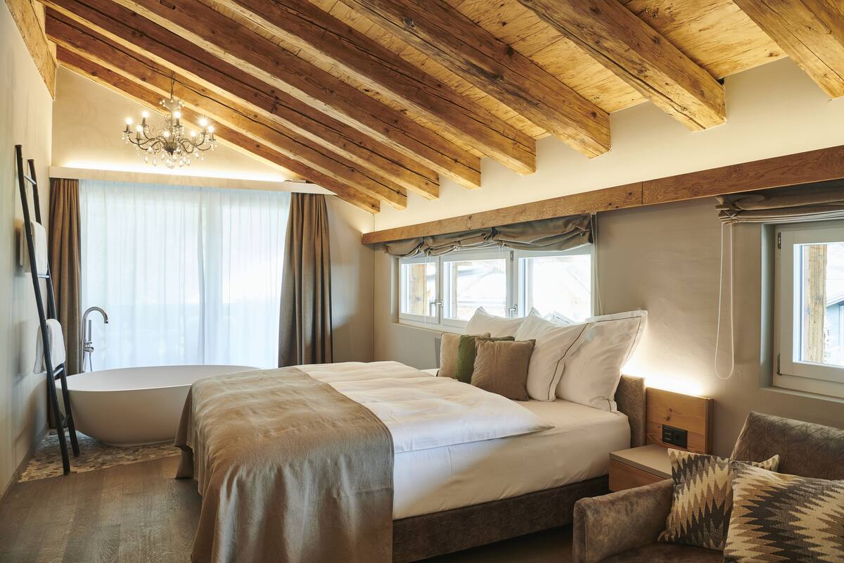 Quarto com cama grande, teto de madeira, banheira e janela com cortinas.