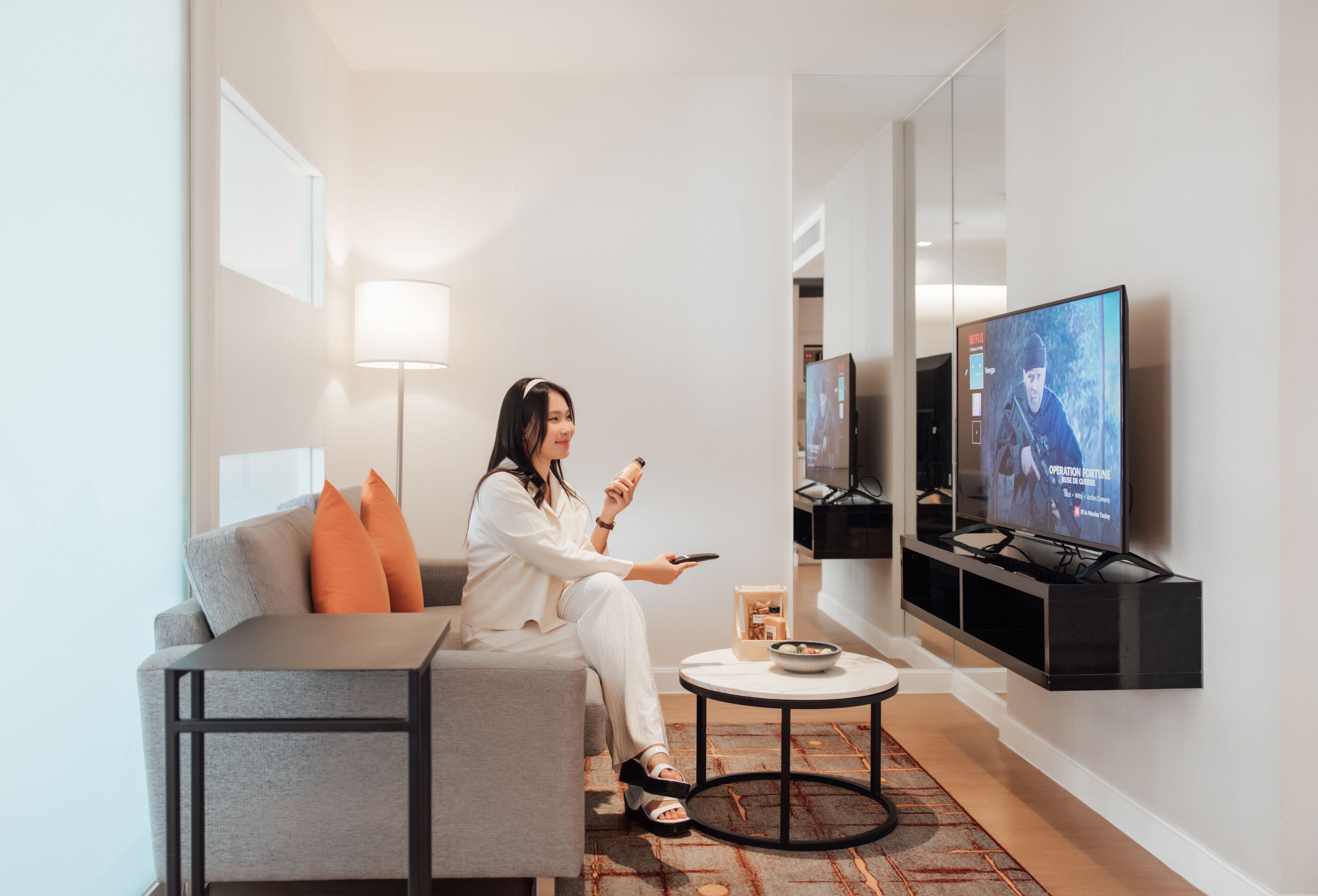 Uma sala de estar moderna com um sofá cinzento, uma mesa de centro redonda e uma televisão de ecrã plano fixada na parede.