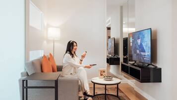 Uma sala de estar moderna com um sofá cinzento, uma mesa de centro redonda e uma televisão de ecrã plano fixada na parede.