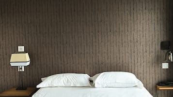 Cama bem arrumada com lençóis brancos, luminária de cabeceira e telefone em mesa de madeira.