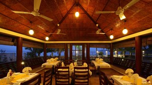 Um restaurante com vigas de madeira no teto, ventiladores de teto e mesas preparadas para refeições, com toalhas de mesa amarelas e guardanapos brancos.