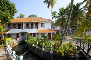 Um edifício branco de dois andares com telhado de telhas, uma varanda e um canal em frente.
