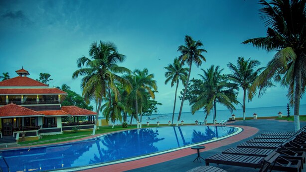 Uma piscina com espreguiçadeiras, palmeiras e um edifício com telhado vermelho.