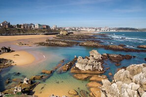 Paisagem costeira com águas claras, formações rochosas e uma praia arenosa.