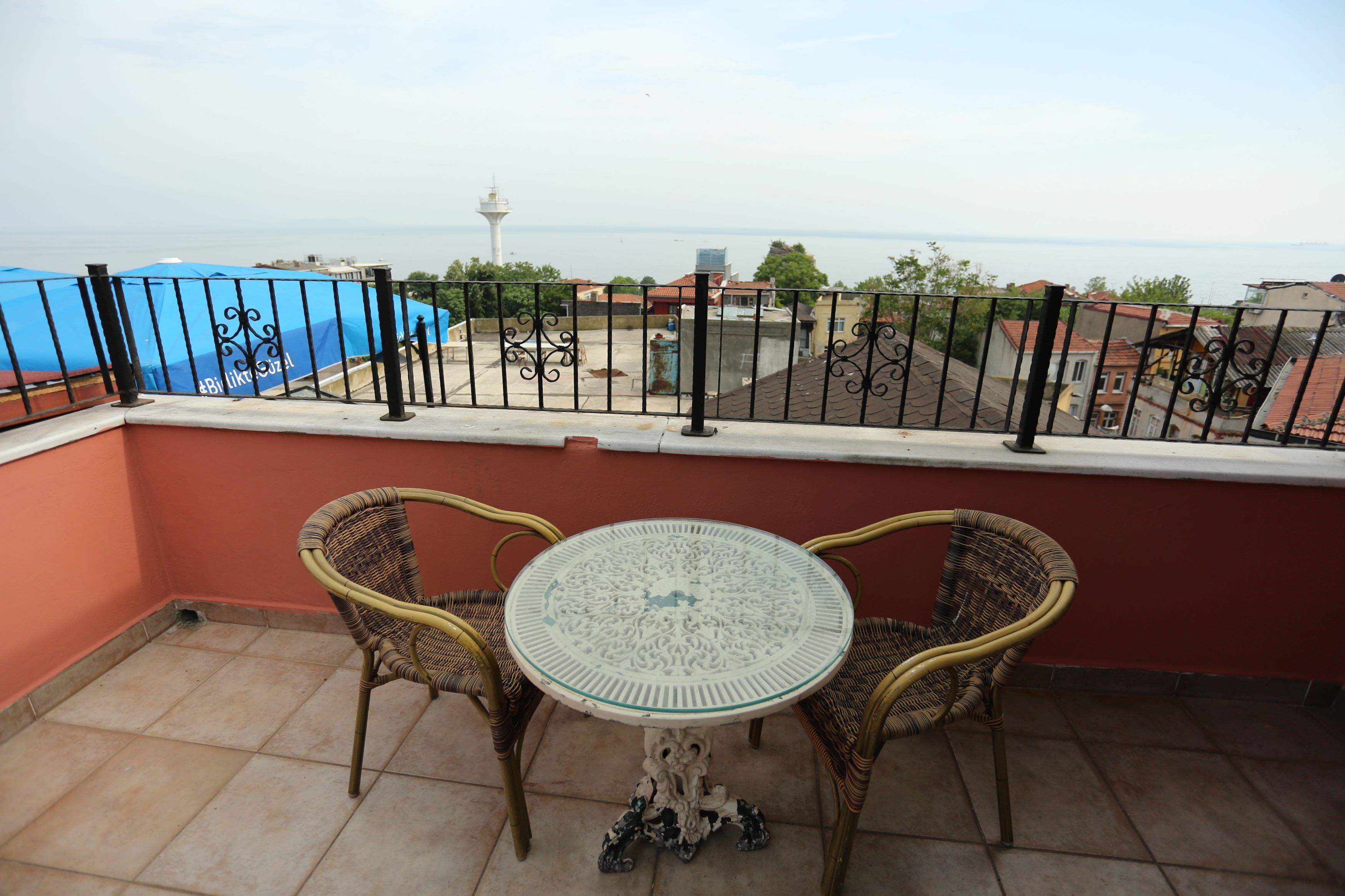 Varanda com uma mesa redonda e duas cadeiras de vime, com vista para o horizonte urbano com edifícios e uma torre ao longe.