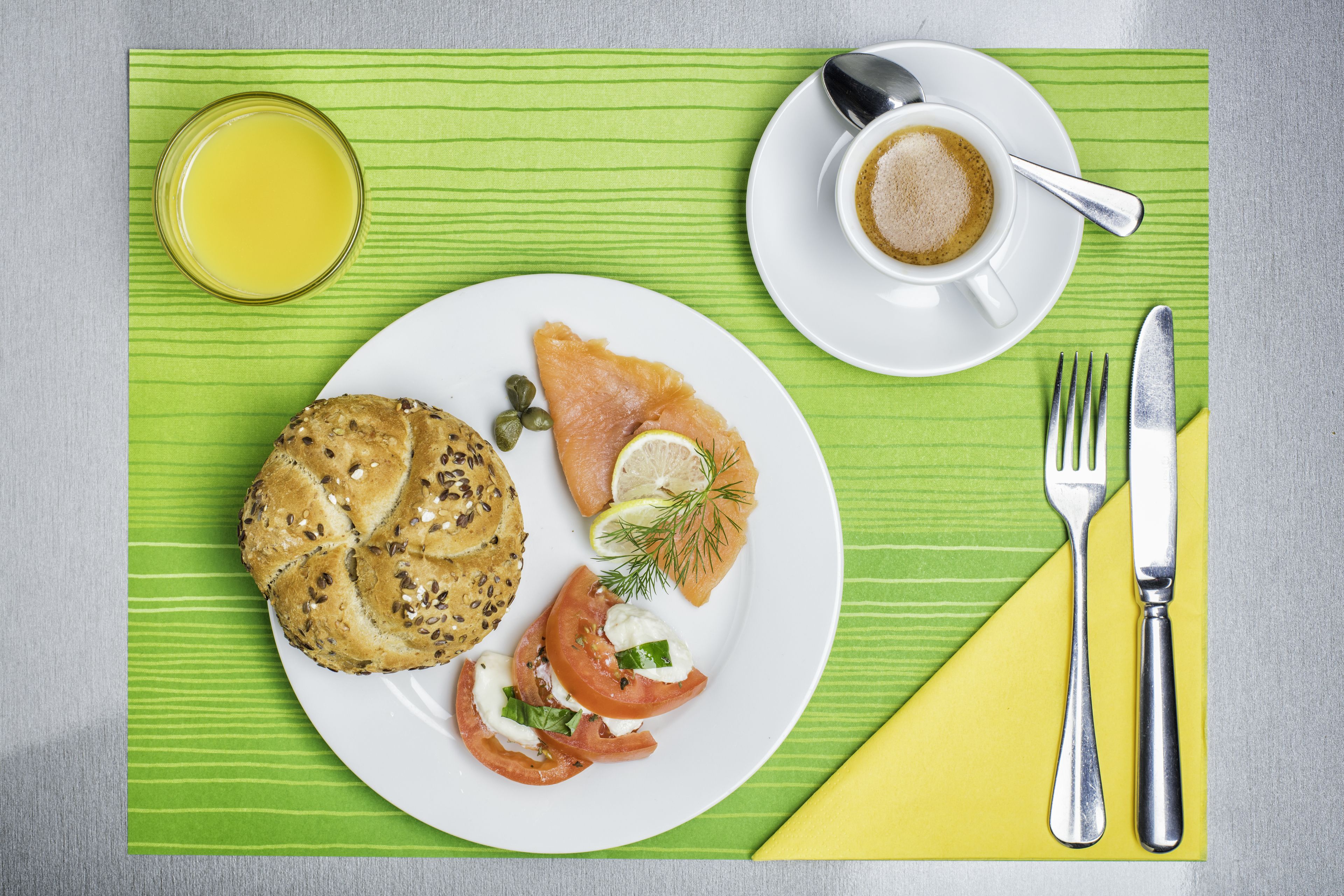 Uma mesa de café da manhã com um prato de comida, um copo de suco e uma xícara de café sobre um jogo americano verde.