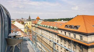 Uma varanda com mesa e cadeiras, com vista para um horizonte urbano com edifícios históricos e o topo de uma igreja.