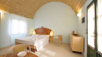 Quarto com cabeceira de madeira, uma cama de solteiro, mesa de cabeceira, uma cadeira, um pequeno armário e janela com cortinas.