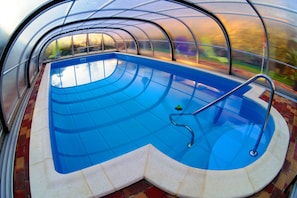 Piscina com cobertura de vidro, água azul cristalina e borda de tijolos.