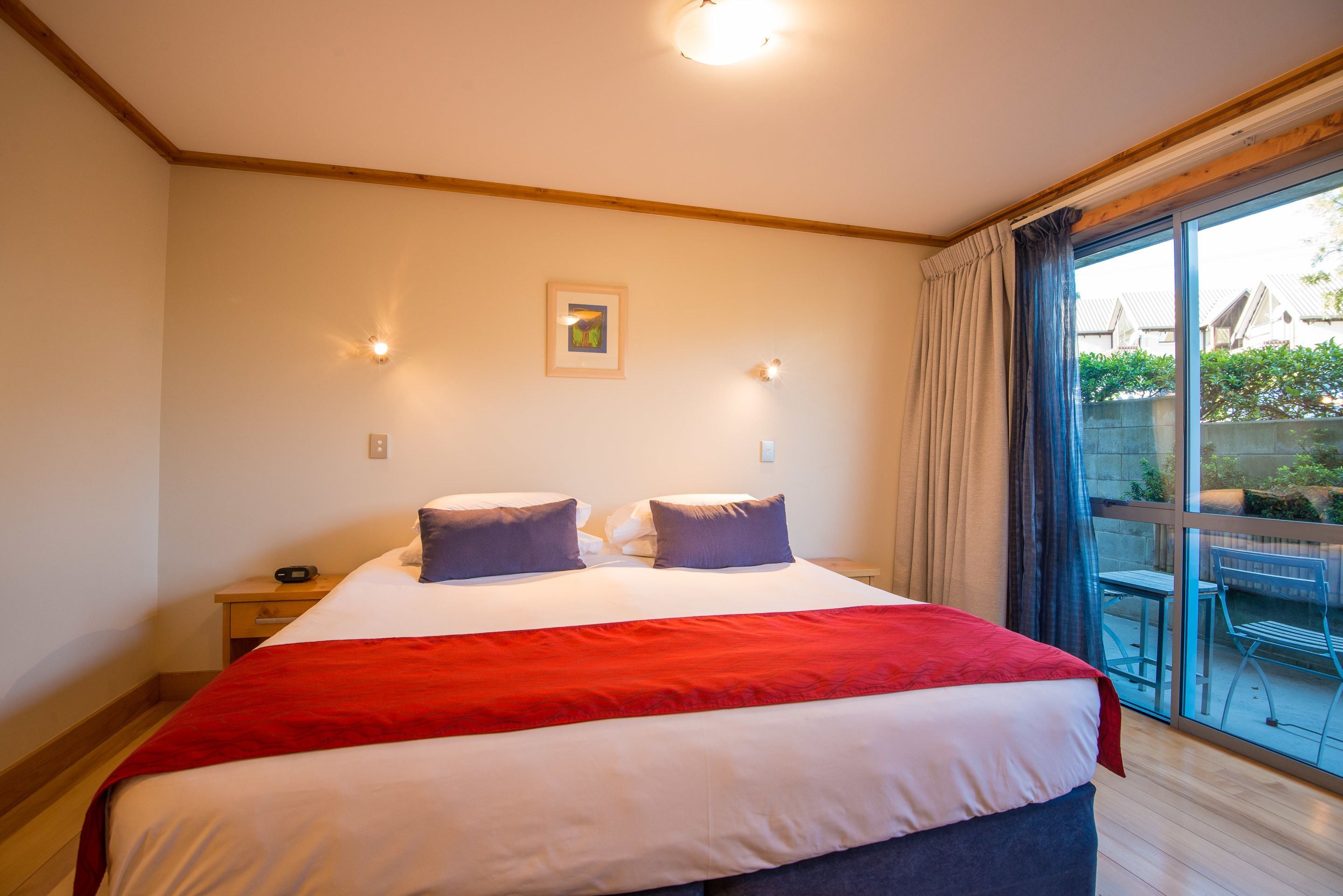 Quarto de hotel com uma cama grande, duas mesas de cabeceira, uma luminária e uma janela com cortinas, oferecendo vista para o exterior.