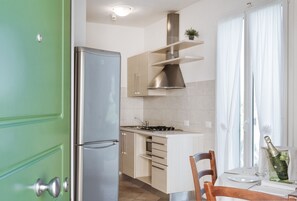 Cozinha moderna com geladeira de aço inoxidável, fogão a gás e armários de madeira. Há uma área de refeições com mesa e cadeiras.