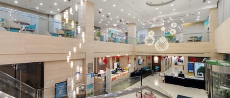 Um hall de hotel em vários níveis, com guarda-corpo de vidro, áreas de estar e balcão de recepção.