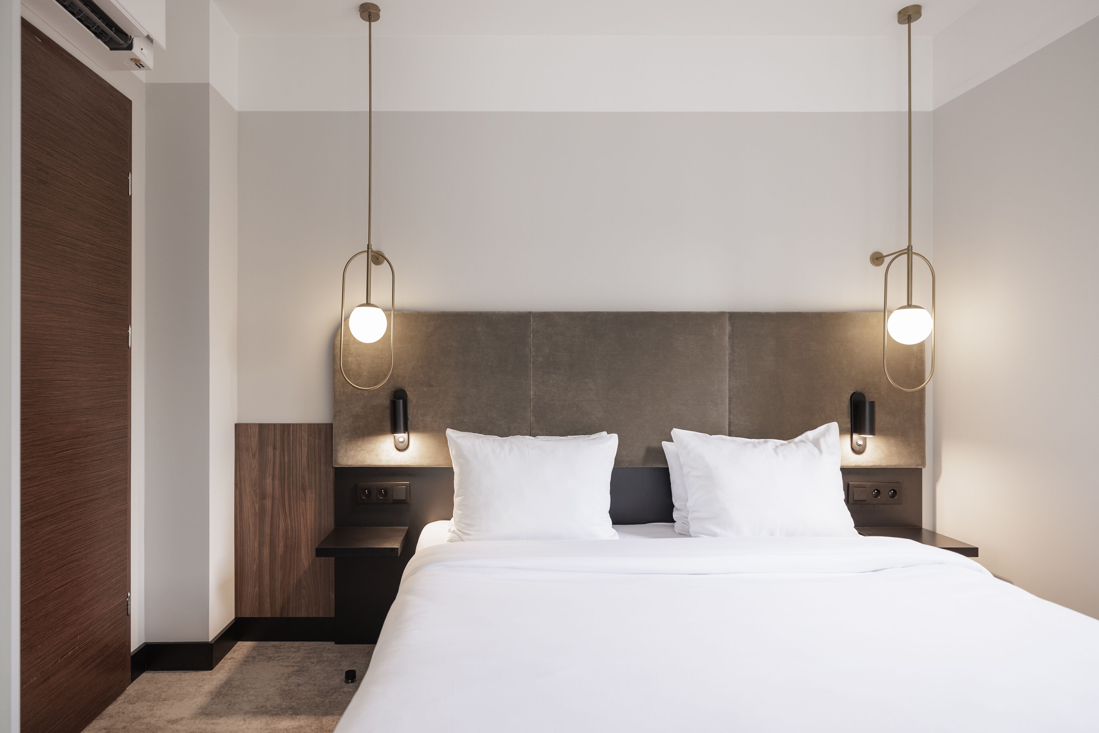 Quarto de hotel moderno com uma cama grande, duas mesas de cabeceira e um guarda-roupa de madeira.